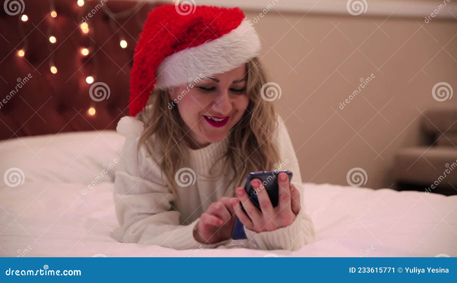 A Woman In A Santa Claus Hat Lies On The Bed And Looks At A Mobile