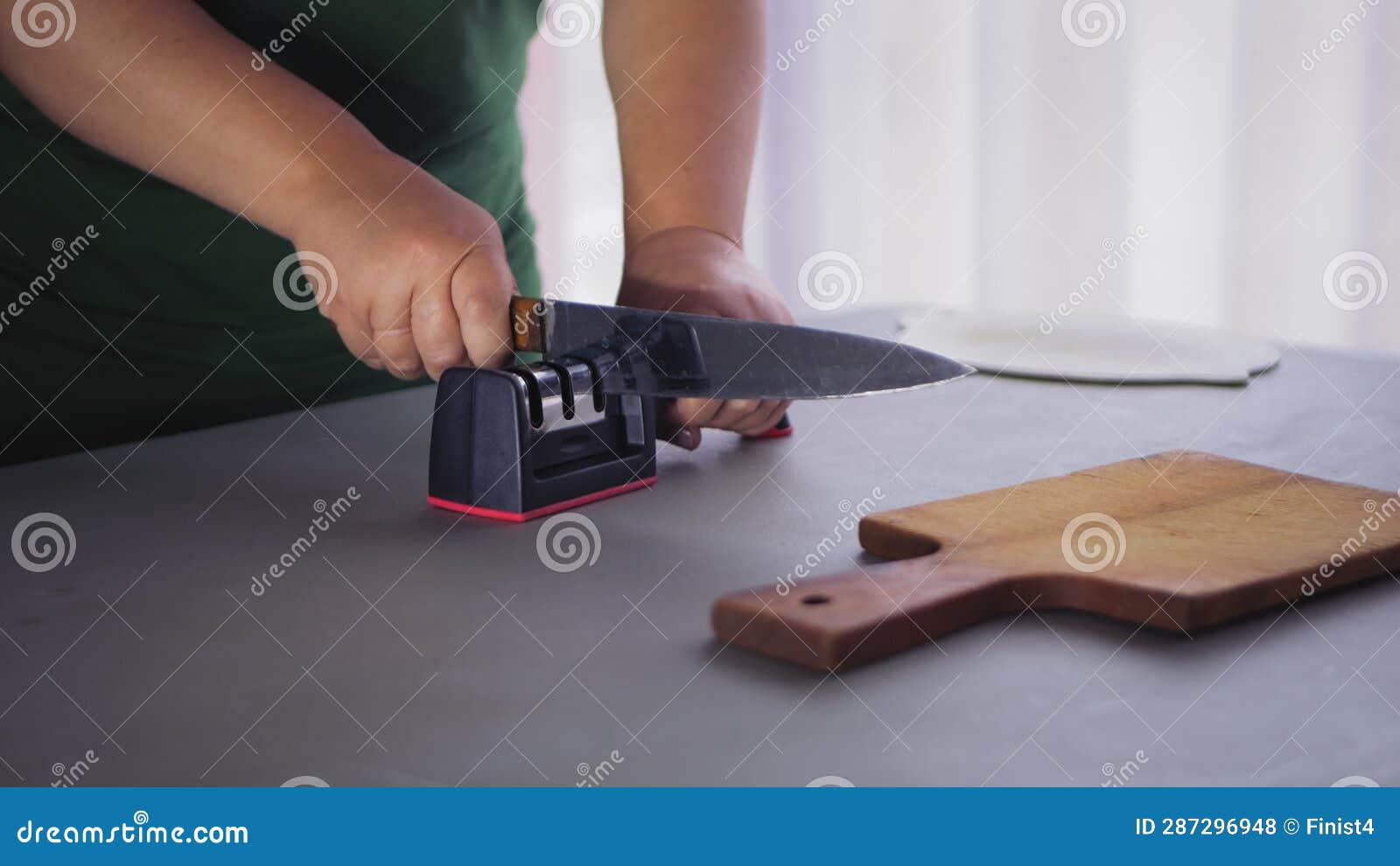 A Woman Sharpens a Kitchen Knife in a Special Knife Sharpener on the ...