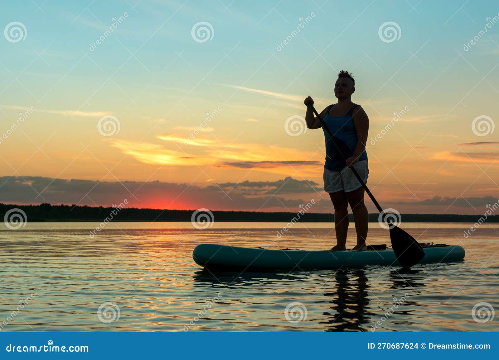 A Woman In Shorts And A T Shirt With A Mohawk Stands On A Sup Board In