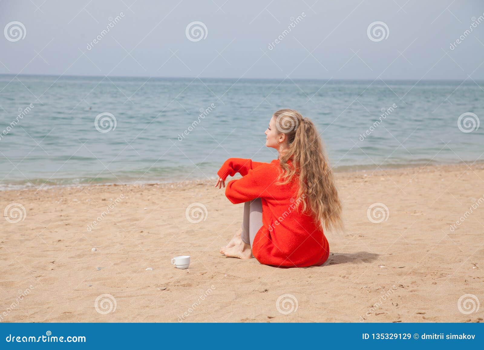 A Woman Sits At A Deserted Sandy Beach Looking At Sea Stock Image