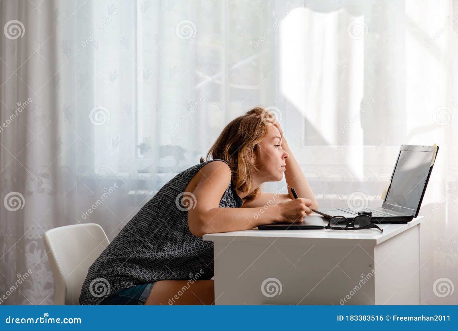 The Woman is Sitting at Her Desk,her Head Propped Up Wearily, Looking ... The Woman is Sitting at Her Desk,her Head Propped Up Wearily, Looking ...