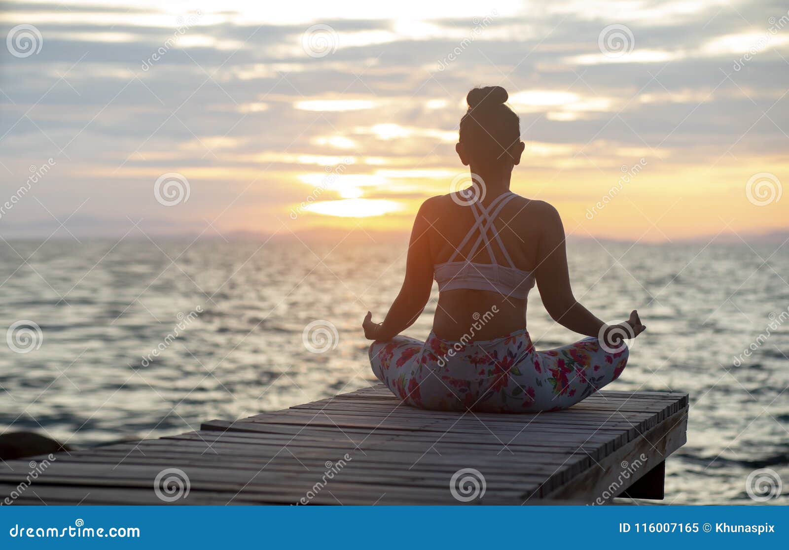 Woman Sitting In Yoga Meditating Pose At Sea Side Against Beautiful Sun