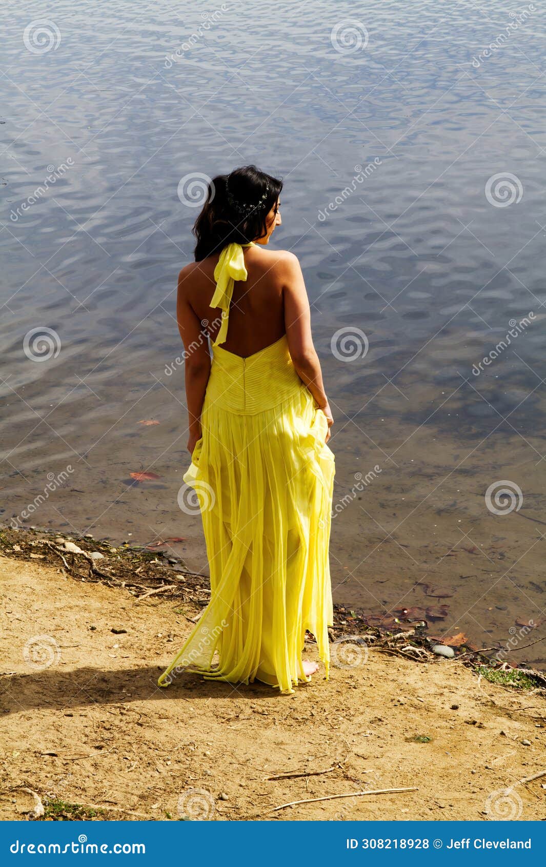 Woman Standing On River Bank Looking At Water In Yellow Dress Stock