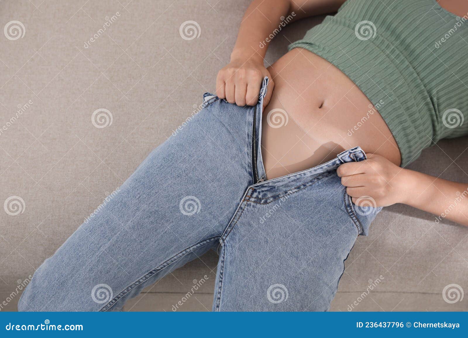 Woman Struggling To Squeeze Into Tight Jeans While Lying On Sofa