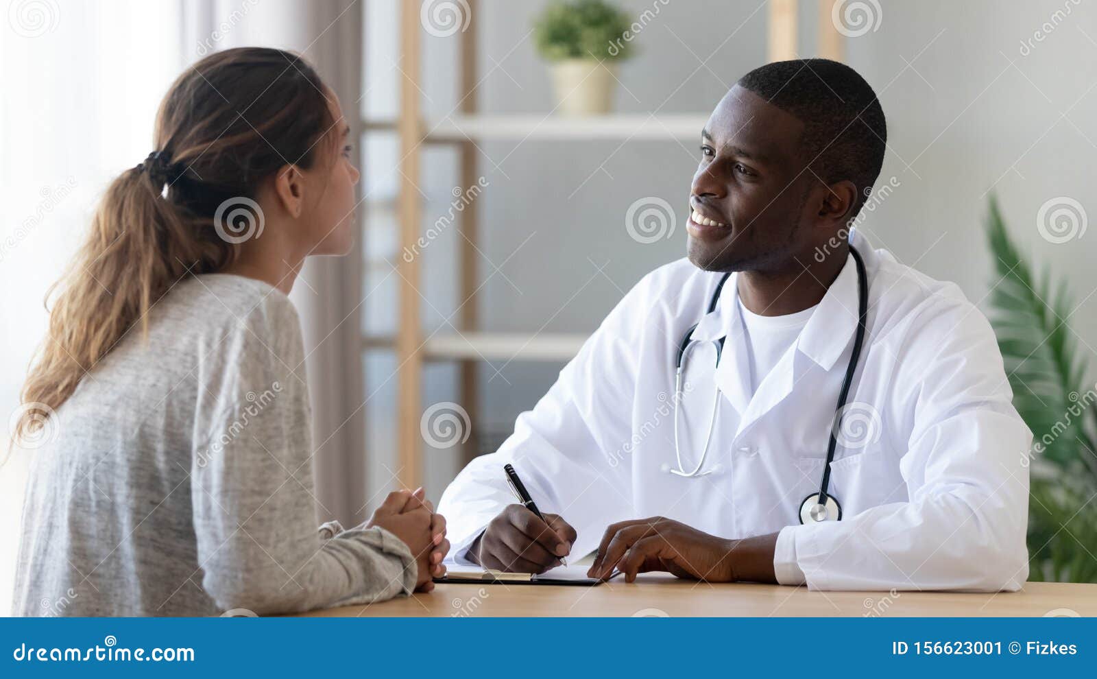 Woman Talking To Smiling African Doctor Noting at Medical Consultation ... Woman Talking To Smiling African Doctor Noting at Medical Consultation ...