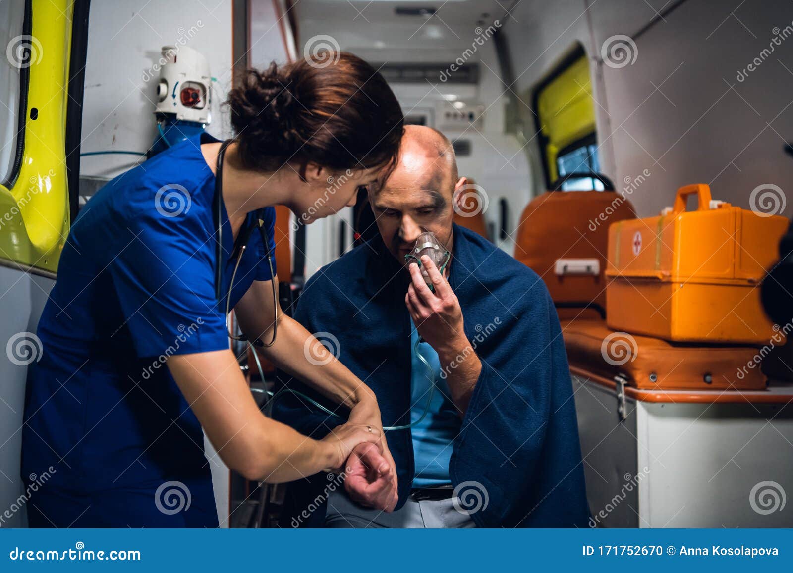 Woman In Uniform Holds A Hand Of Man Who Sits In Oxygen Mask In Blanket