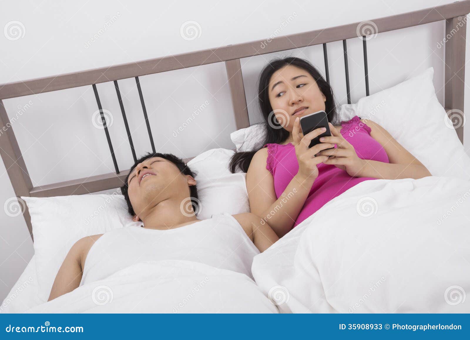 Woman Using Cell Phone while Looking at Man Sleeping in Bed Stock Image ...