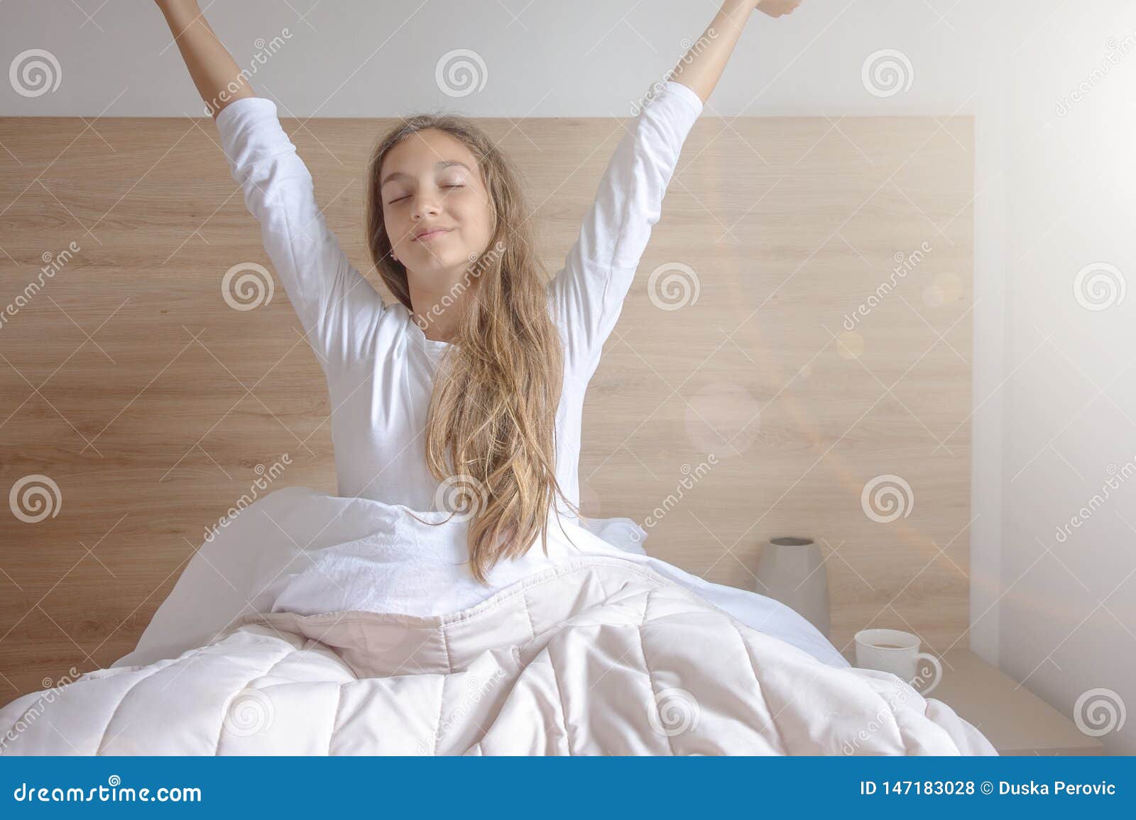Woman Waking Up And Stretching Her Arms Sitting On Bed At Home In The