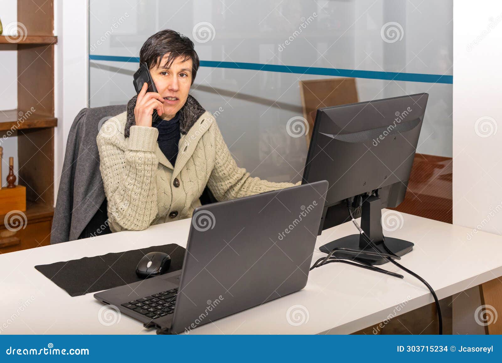 A Woman Working in Office in Front of Two Computers, Talking on Phone ...