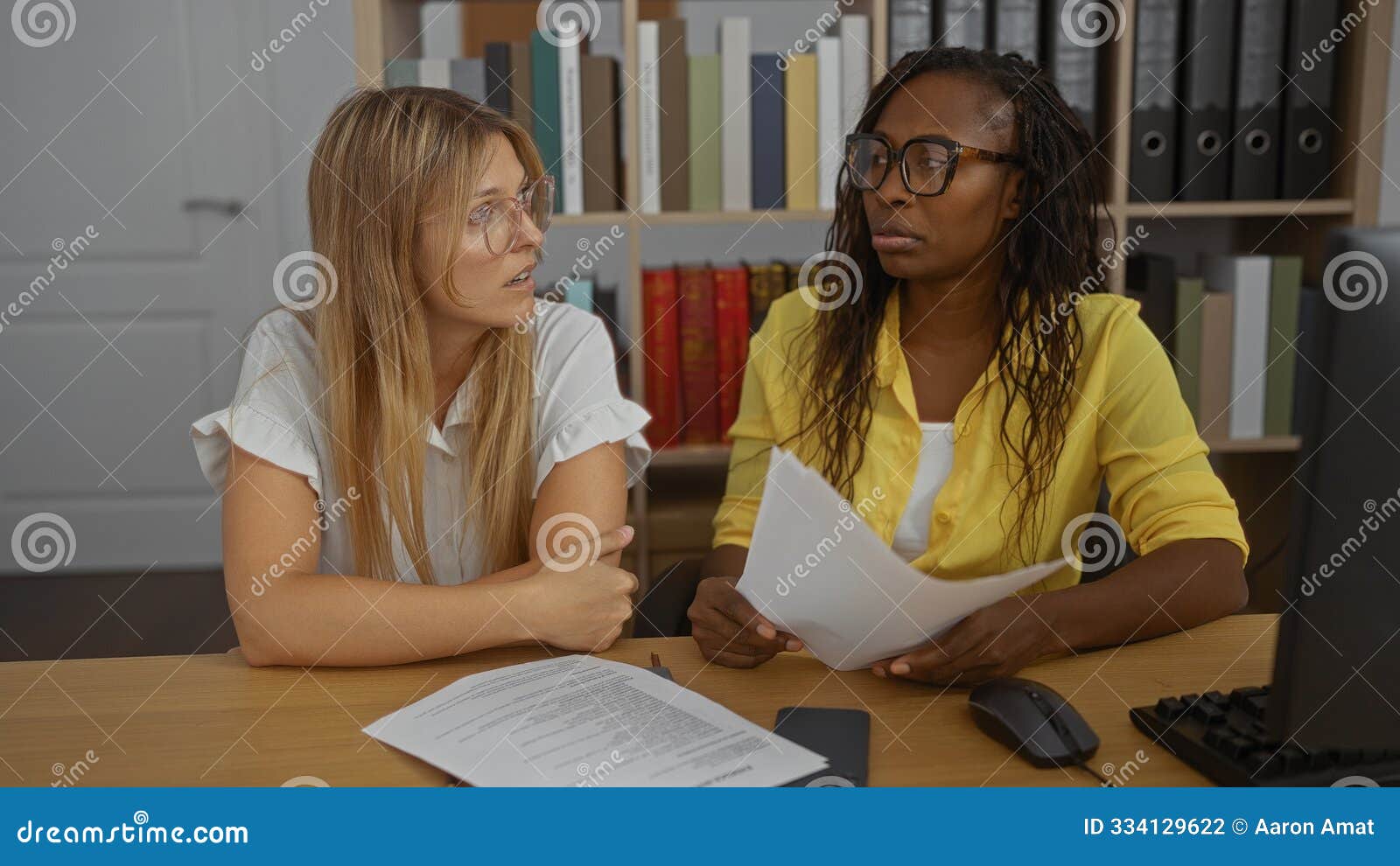 Women Discussing Business Documents at an Office Table with Books and ...