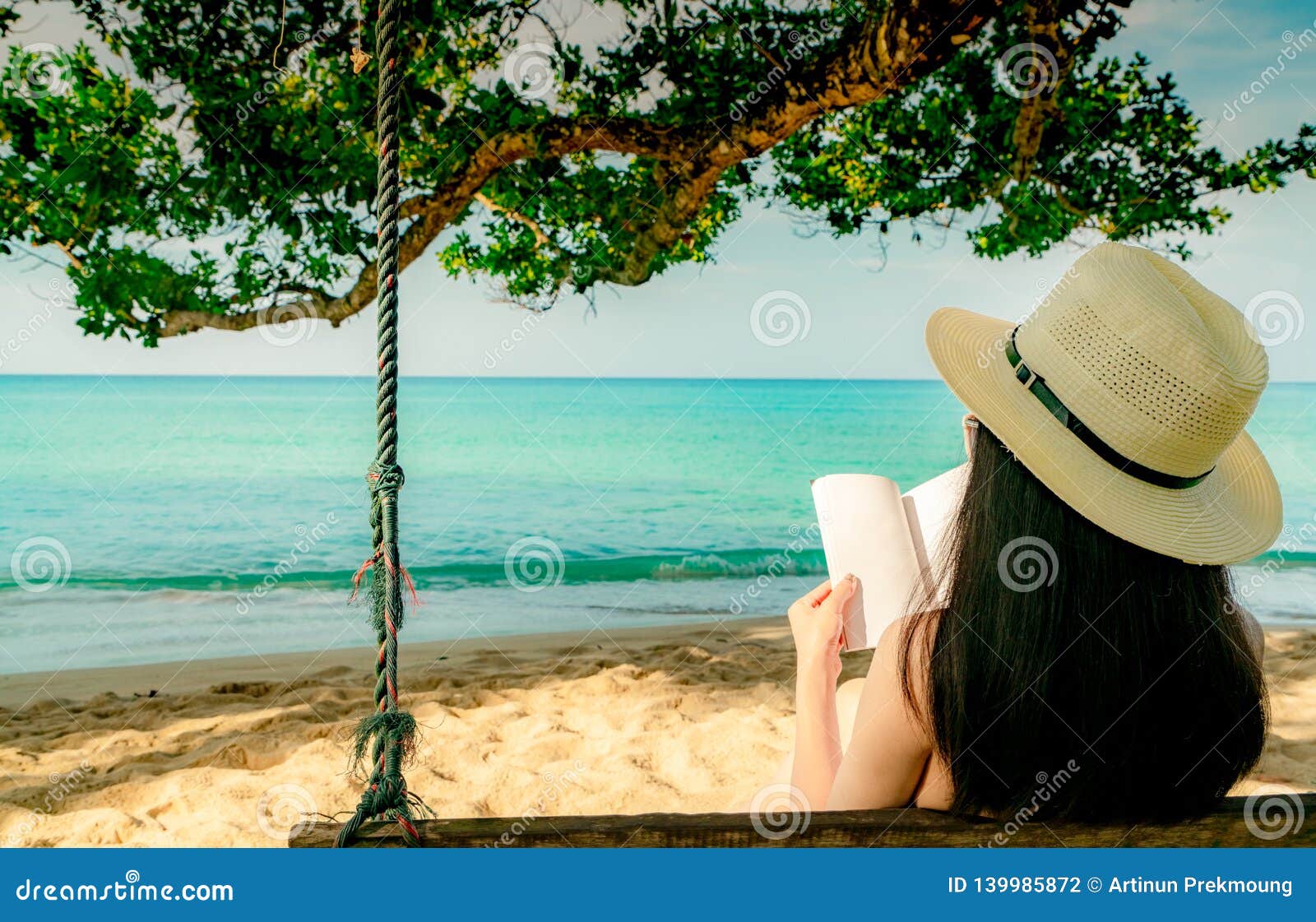 Women Sit And Reading A Book On Swings Under The Tree By The Sea Back