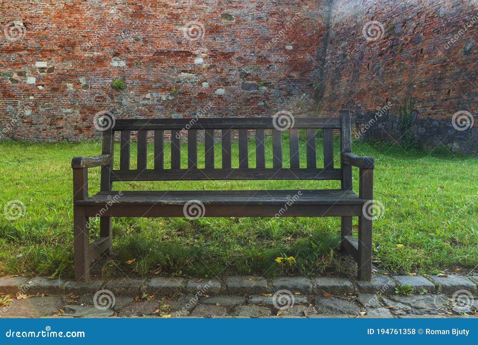 A Wooden Bench by the Footpath Stands on the Grass. Behind the Bench is ...
