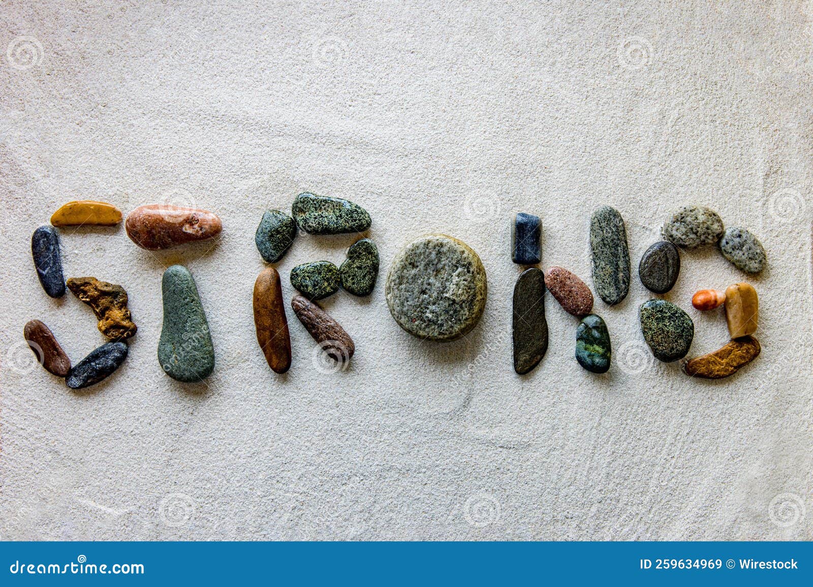 Word STRONG is Written Using Colored Stones on a White Sand Surface ...