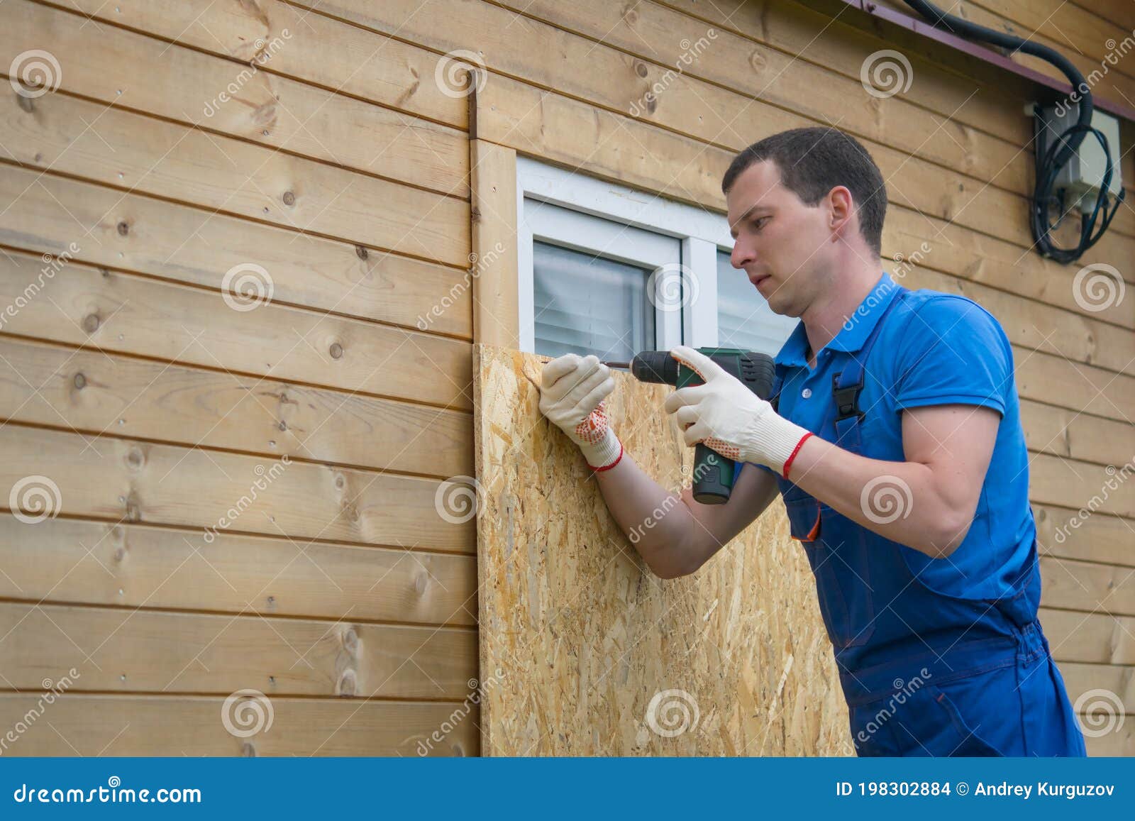 A Worker in a Blue Uniform, Blocks the Window of the House with a ...