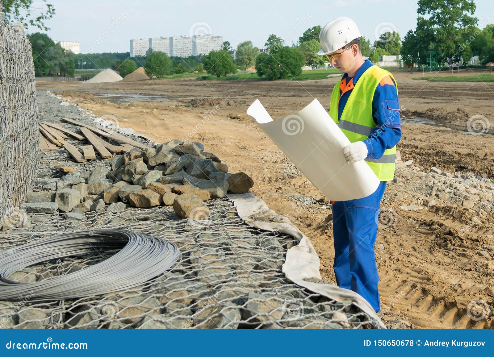 A Worker at a Construction Site Looks at a Construction Plan on a Large ...