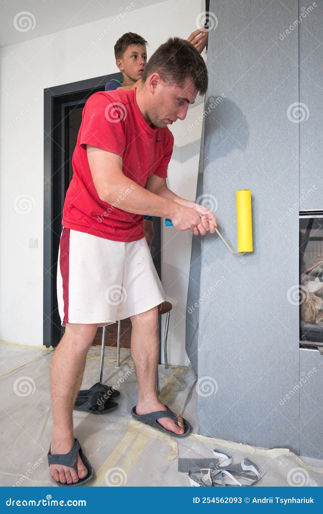 A Worker Glues Wallpaper on the Wall with a Fireplace Using a Rubber ...
