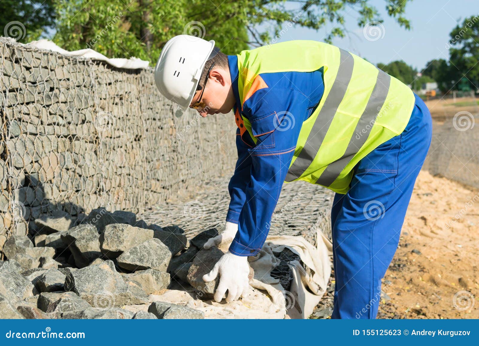 A Worker in Overalls at a Construction Site Raises a Stone from the ...