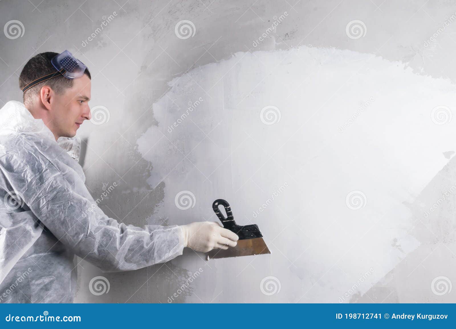 A Worker in Protective Clothing Finishes a Concrete Wall with Putty ...