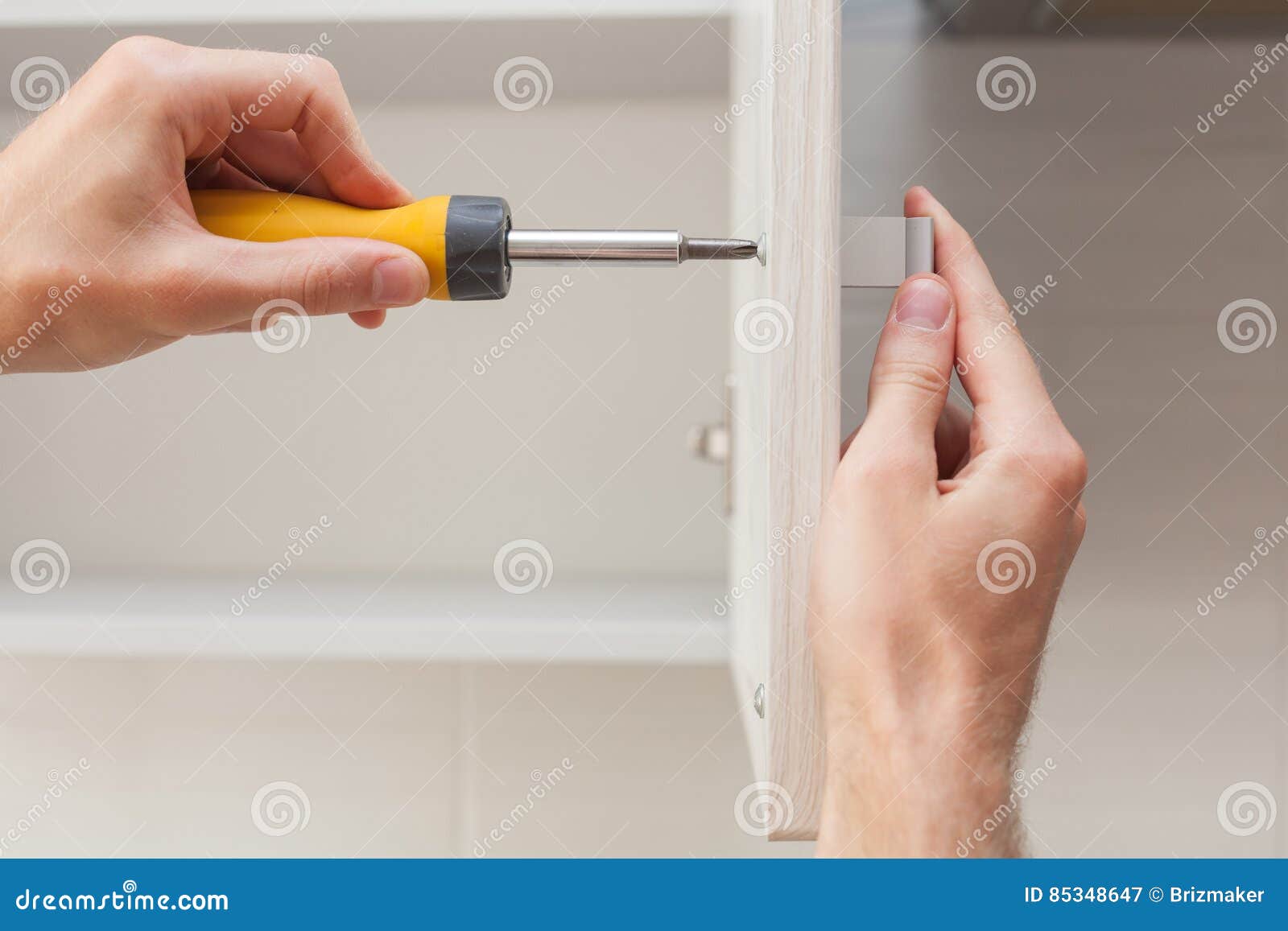 The Worker Sets a New Handle on the White Cabinet with a Screwdriver ...