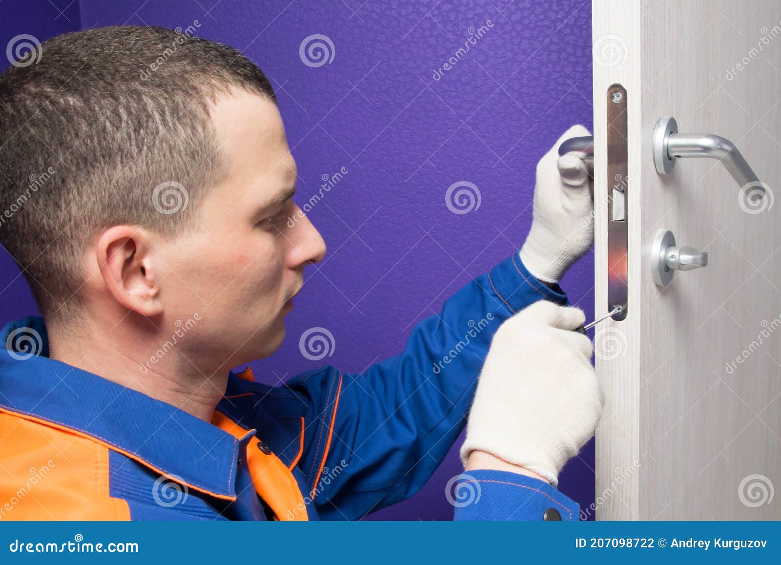 A Worker in Uniform Repairs the Door Lock for Proper Operation Stock ...