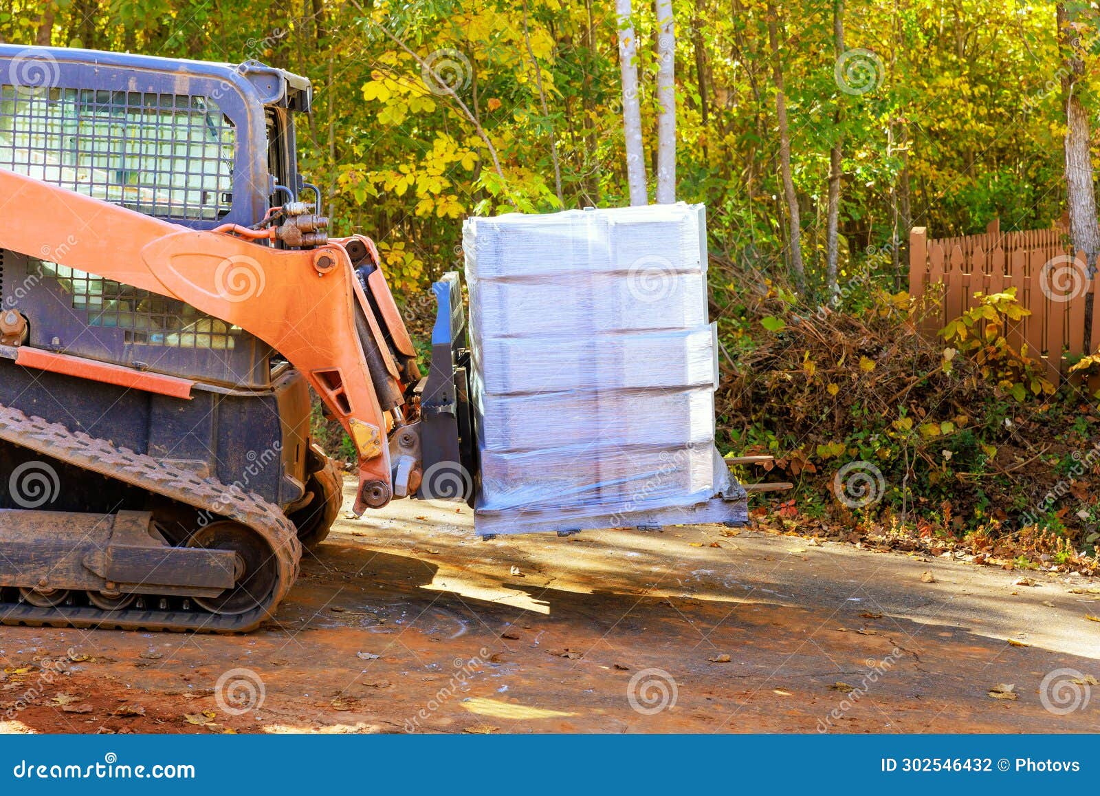 Worker Is Unloading Pallets Of Concrete Blocks For Retaining Wall While Using A Small Tractor