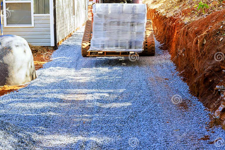 A Worker Unloads Pallets Of Concrete Blocks For Retaining Wall With Aid Of Small Tractor Stock