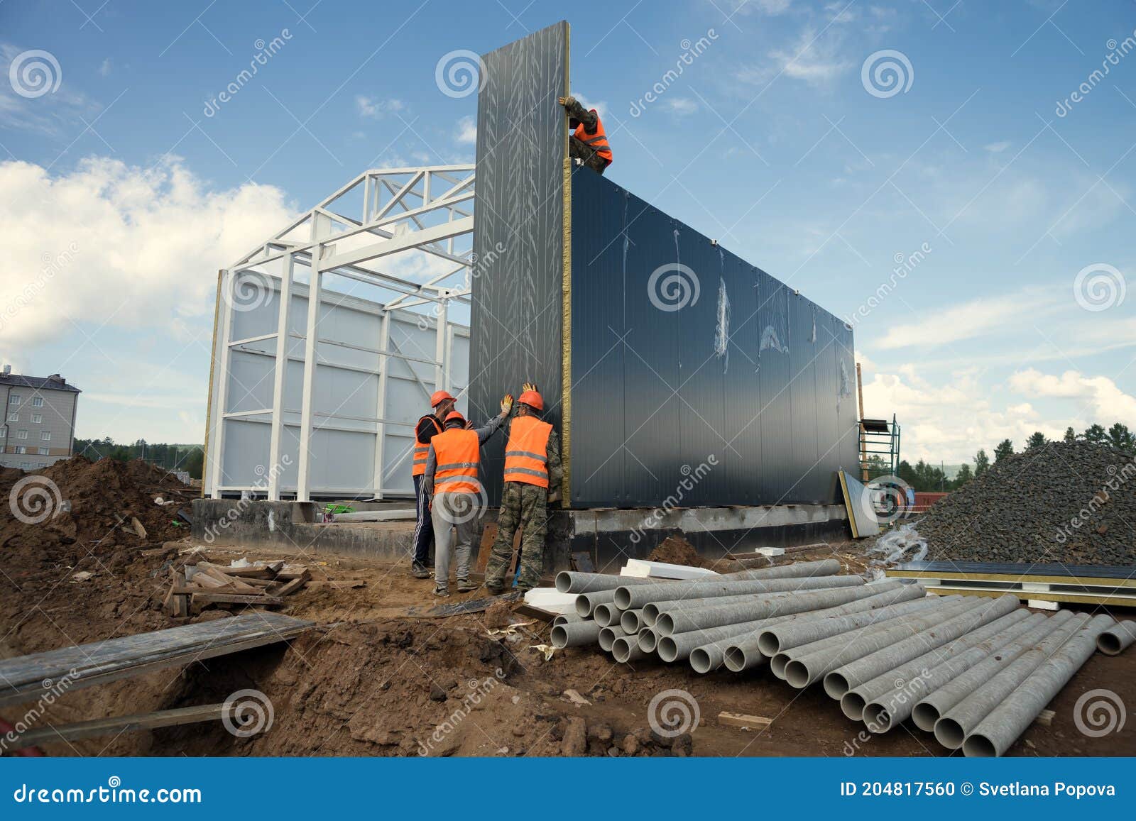 Workers in Hard Hats Install a Wall Panel on the Frame of an Industrial ...