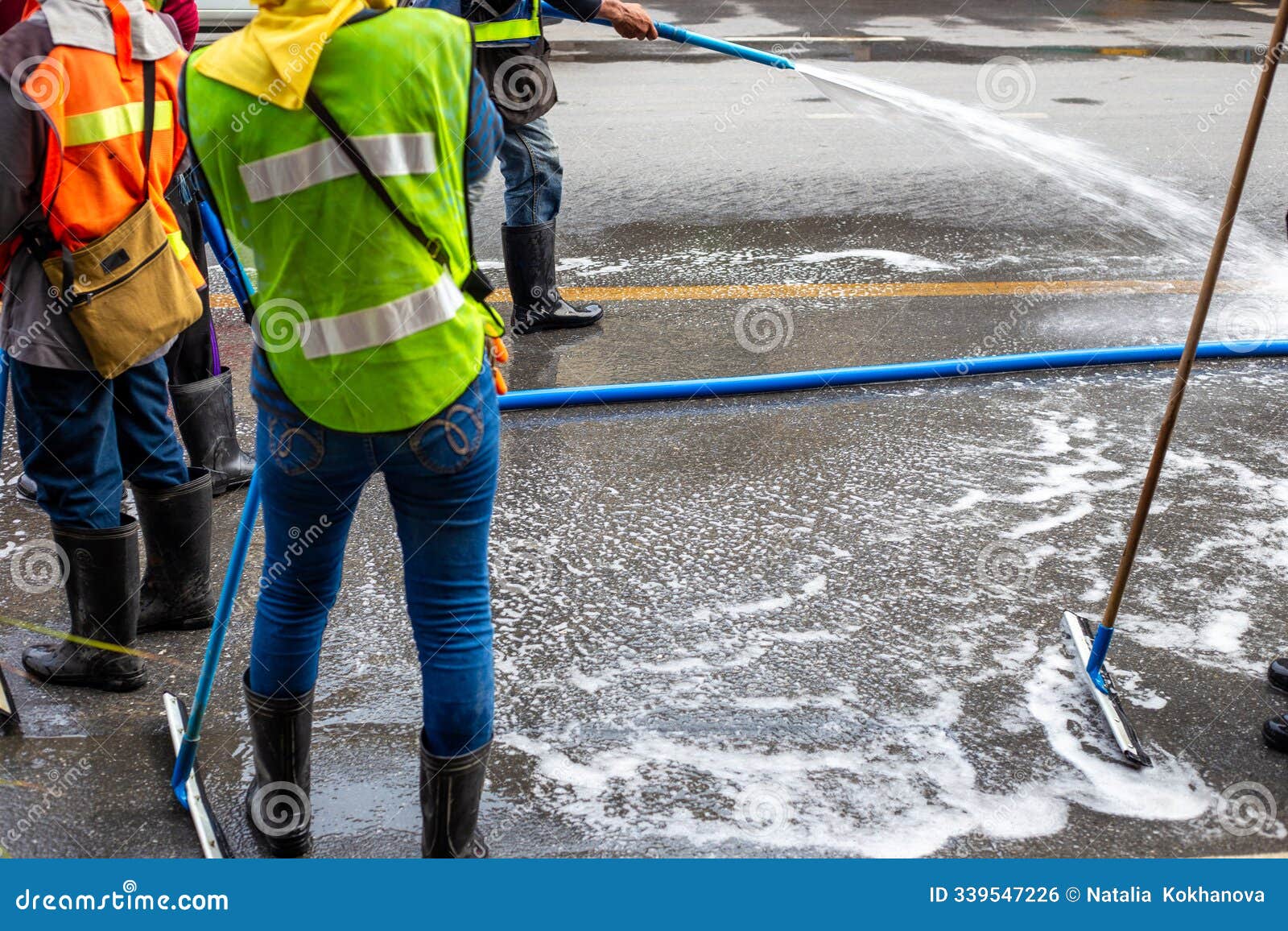 Workers in Rubber Boots with Hoses in Their Hands Wash the Road Surface ...