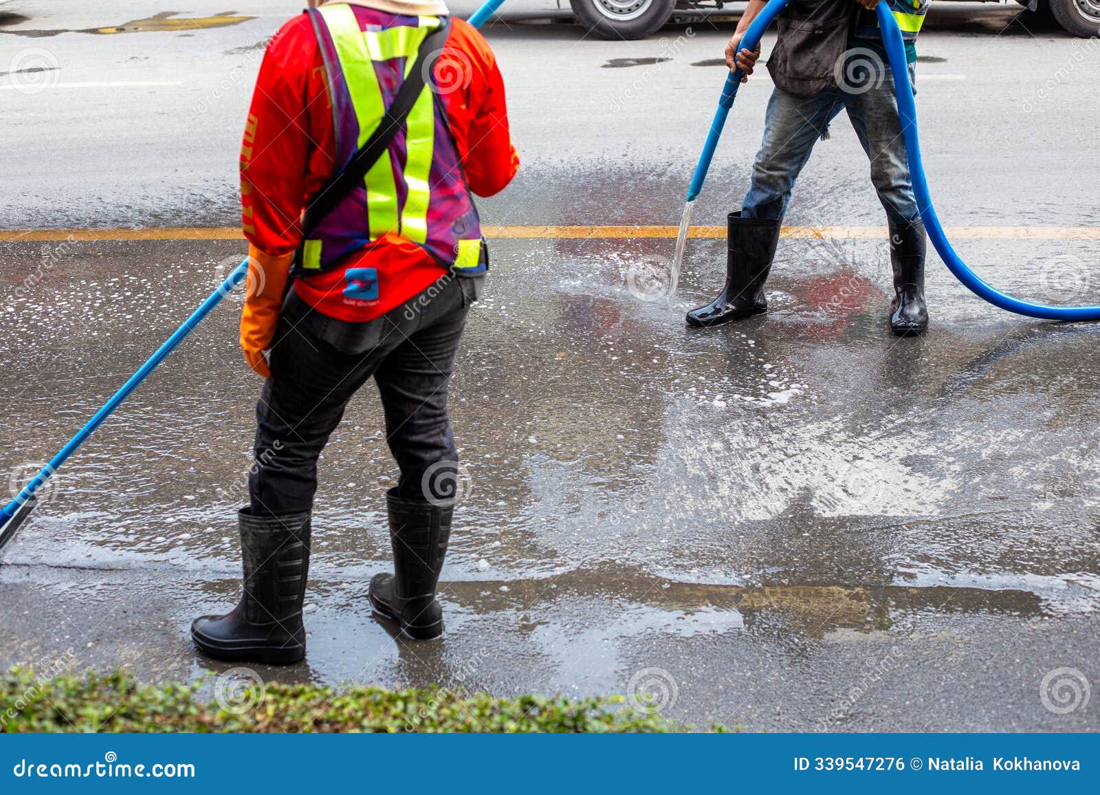 Workers in Rubber Boots with Hoses in Their Hands Wash the Road Surface ...