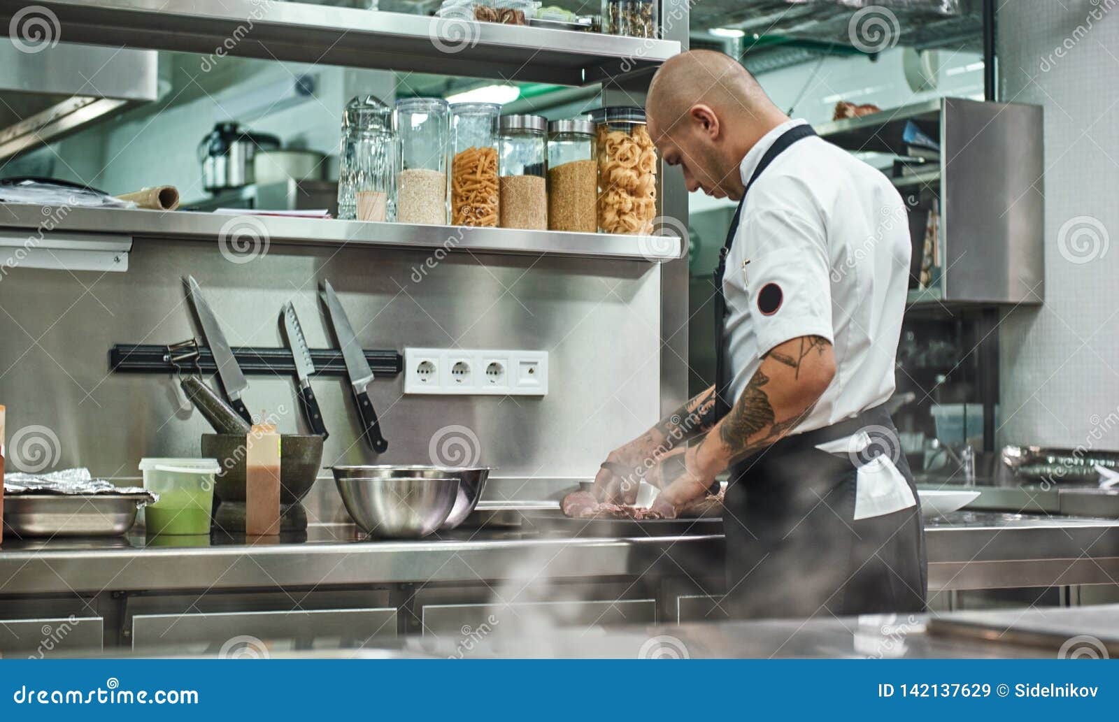 Working Process. Back View of Male Chef in Apron and with Tattoos on ...