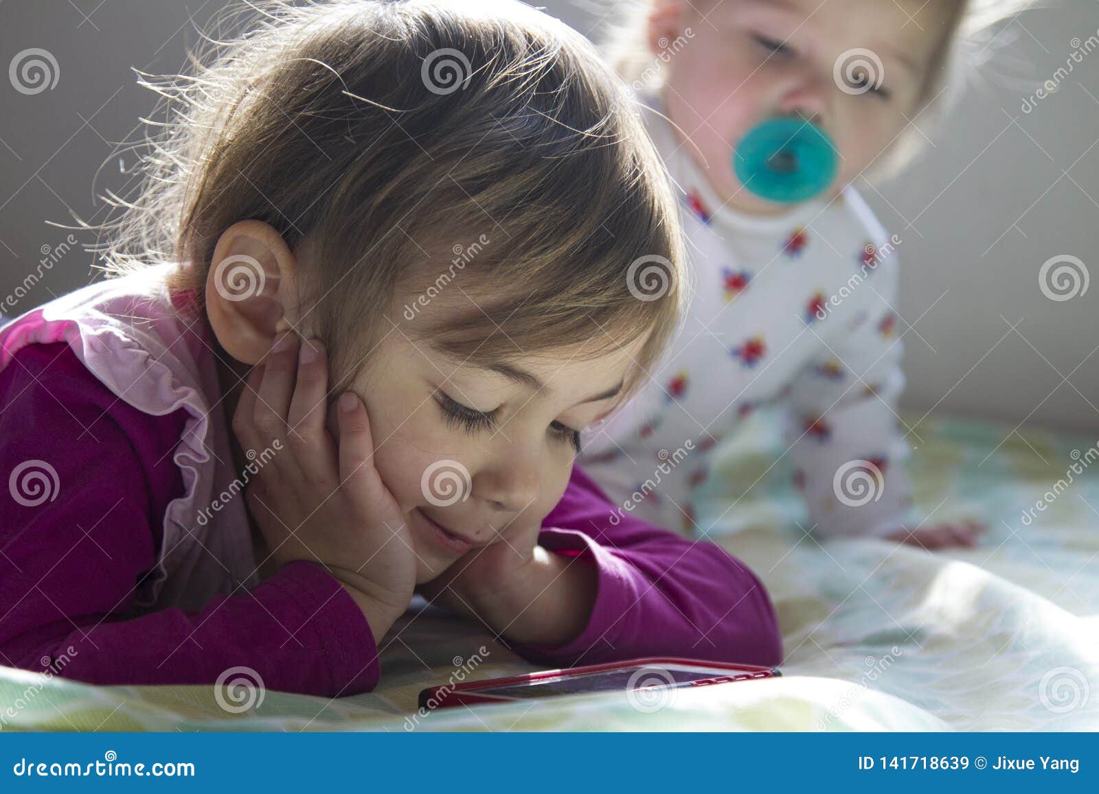4-year-old Girl Watching Tablet and 1-year-old Girl Looking Aside Stock ...