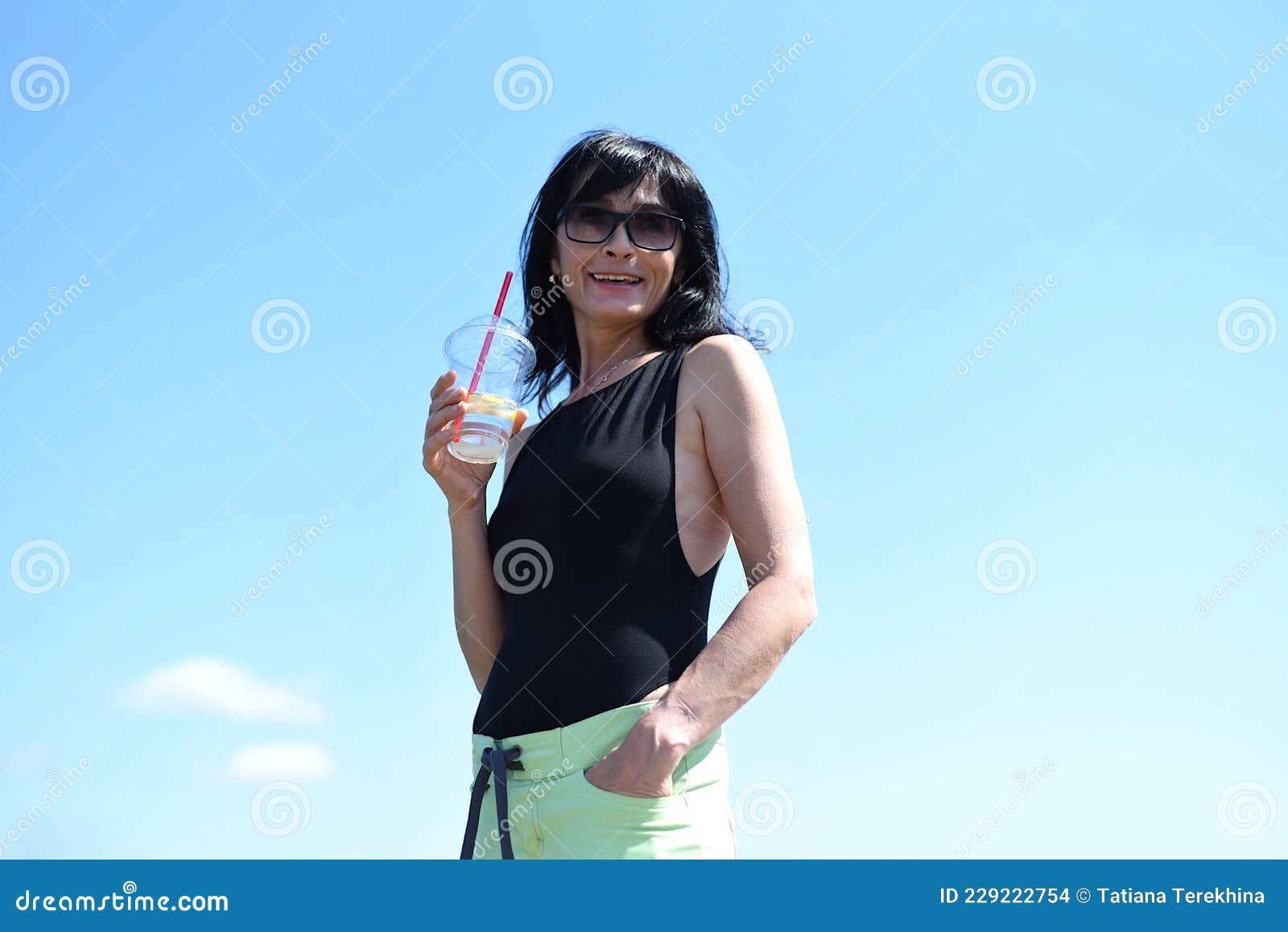 45 Years Old Russian Woman Drinking Lemonad And Standing Against Blue
