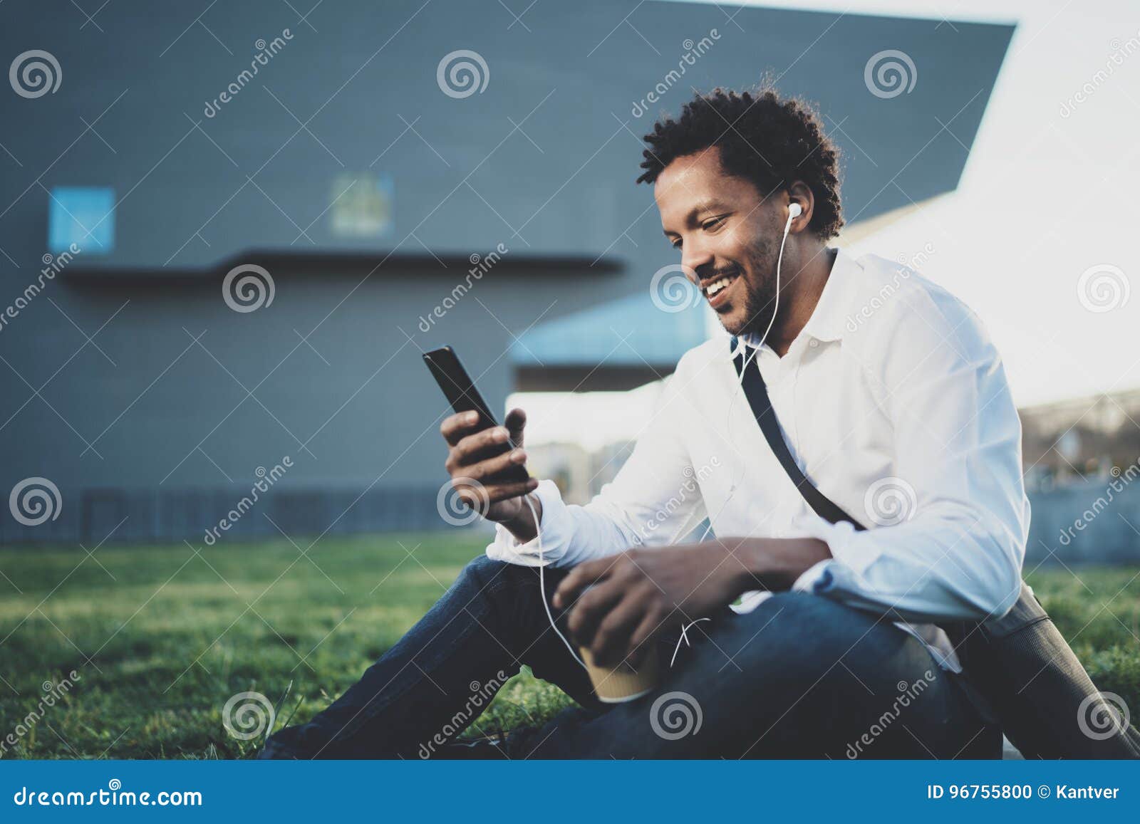 Young African American Man In Headphone Sitting At Sunny City Park And