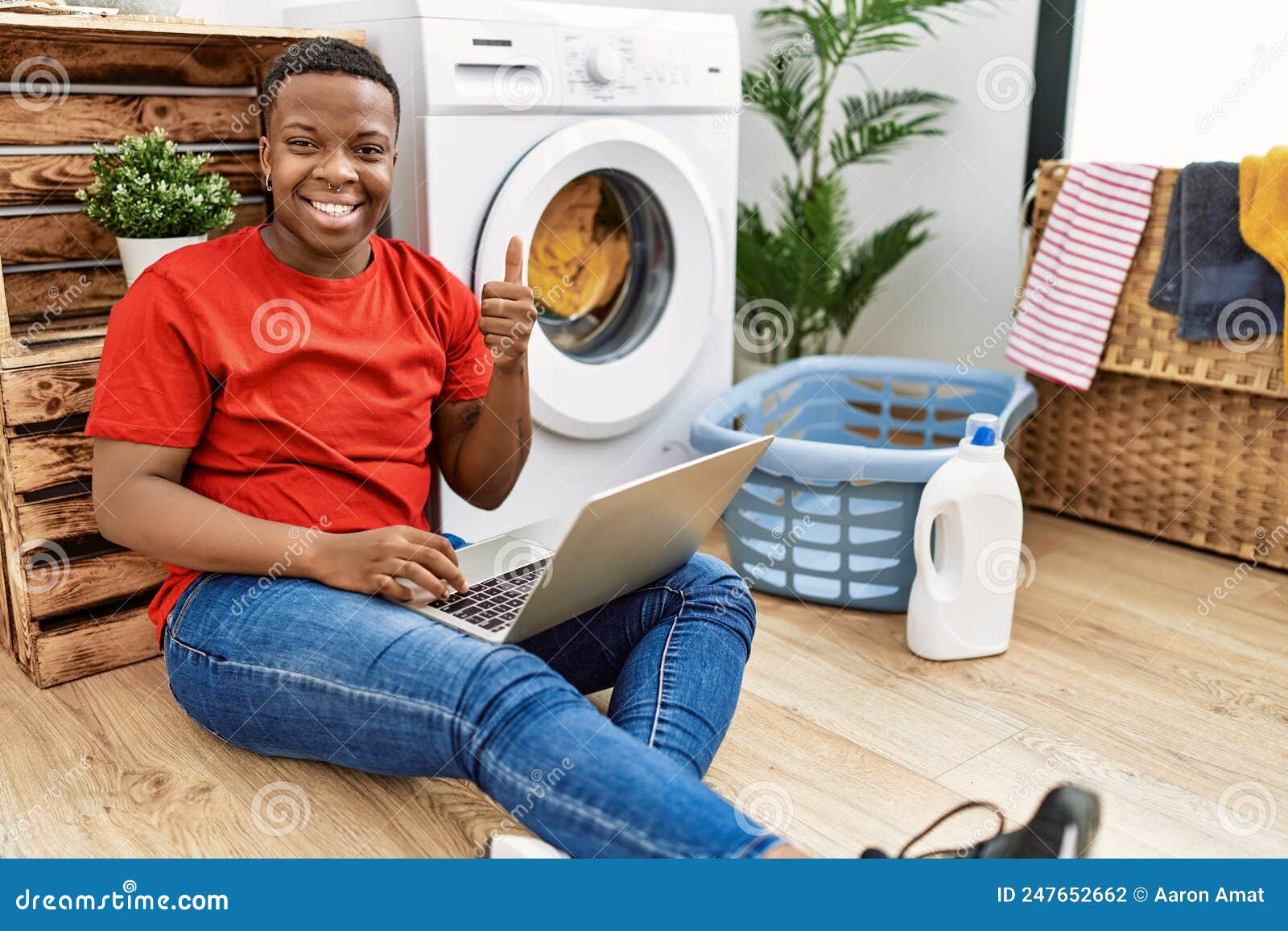 Young African Man Doing Laundry and Using Computer Doing Happy Thumbs ...