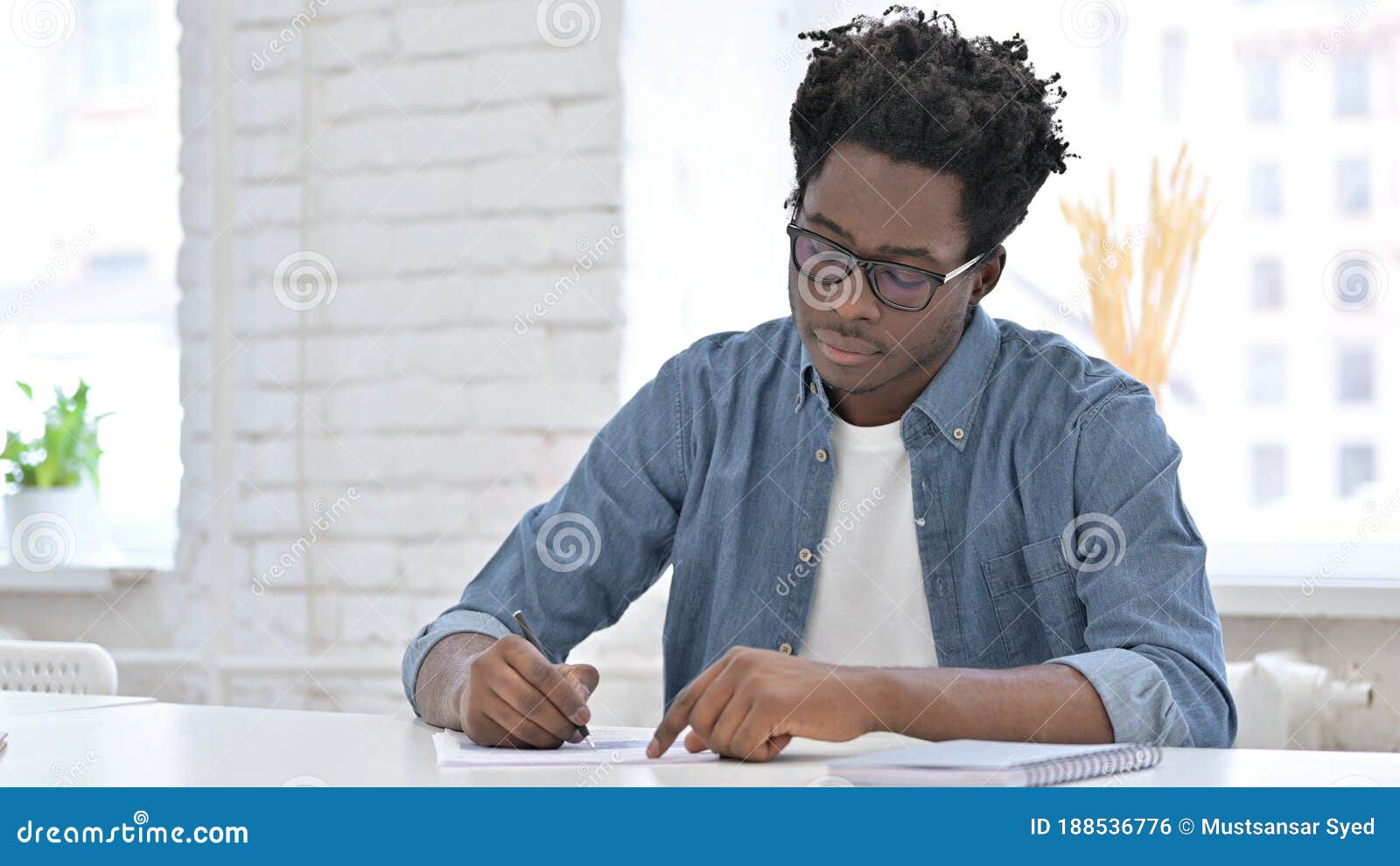 Young African Man Writing on Document in Office Stock Photo - Image of ...