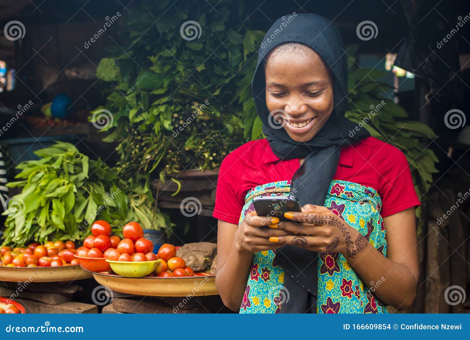 Young African Woman Selling In A Local Market Smiling While Using Her