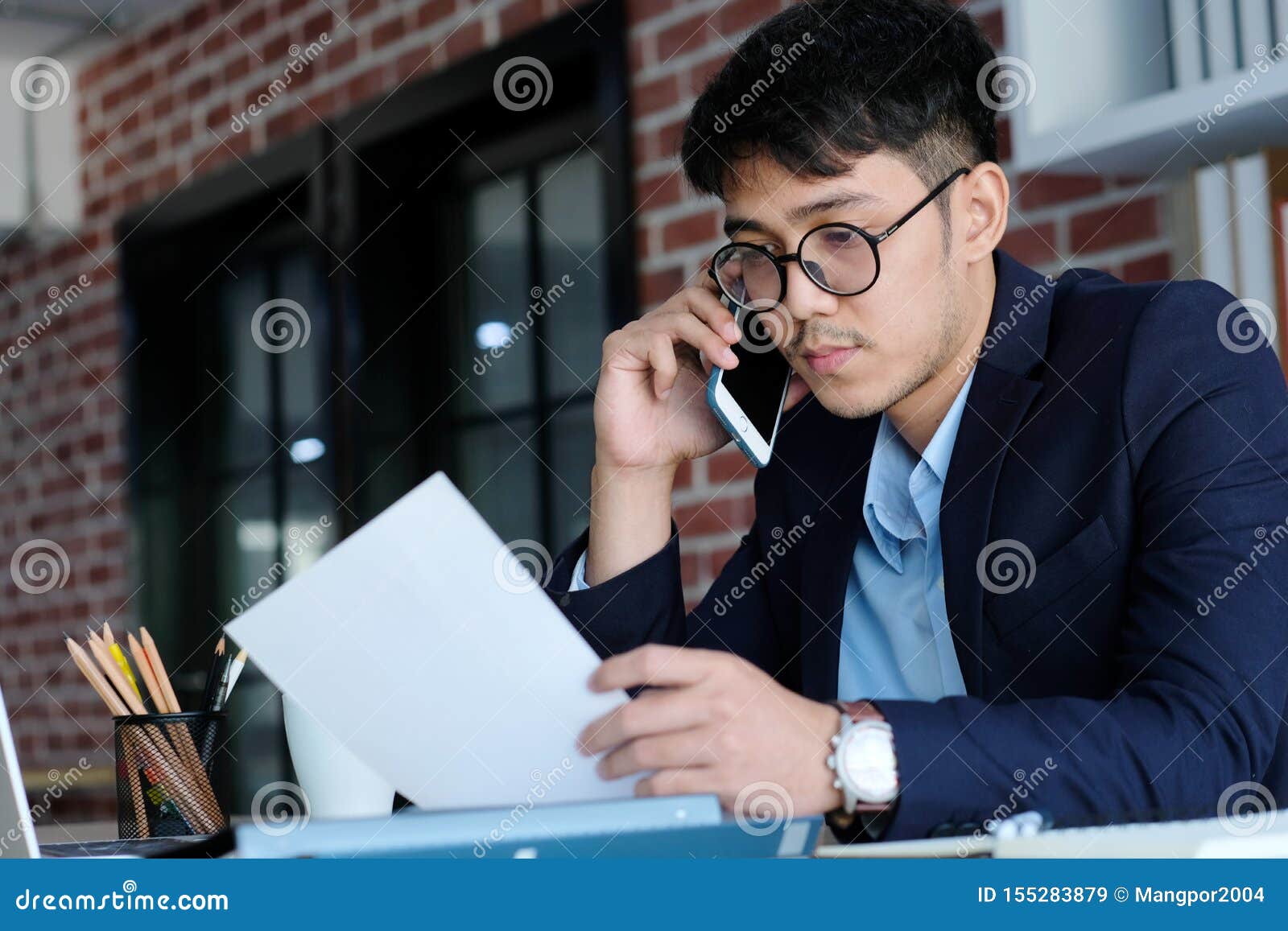 Young Asian Businessman Reading Papers Talking Phone at Office ... Young Asian Businessman Reading Papers Talking Phone at Office ...