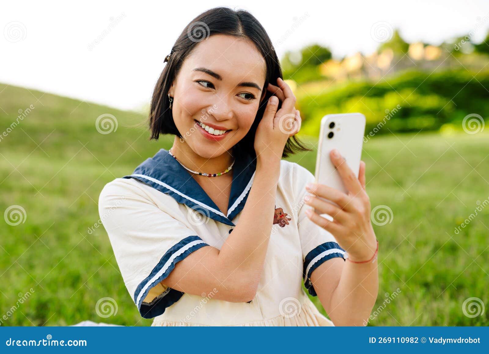 Young Asian Girl Taking Selfie On Mobile Phone While Sitting In Green