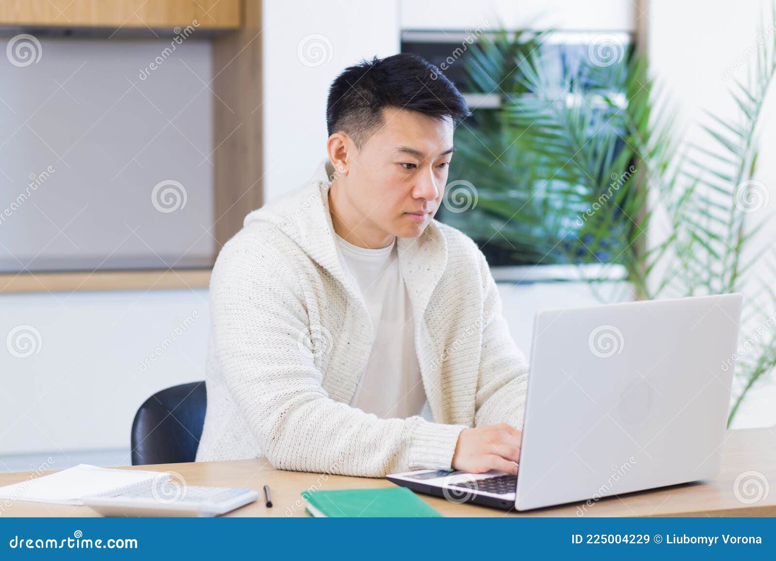 Asian Man Working at Home on a Laptop Computer Sitting at a Table in ...