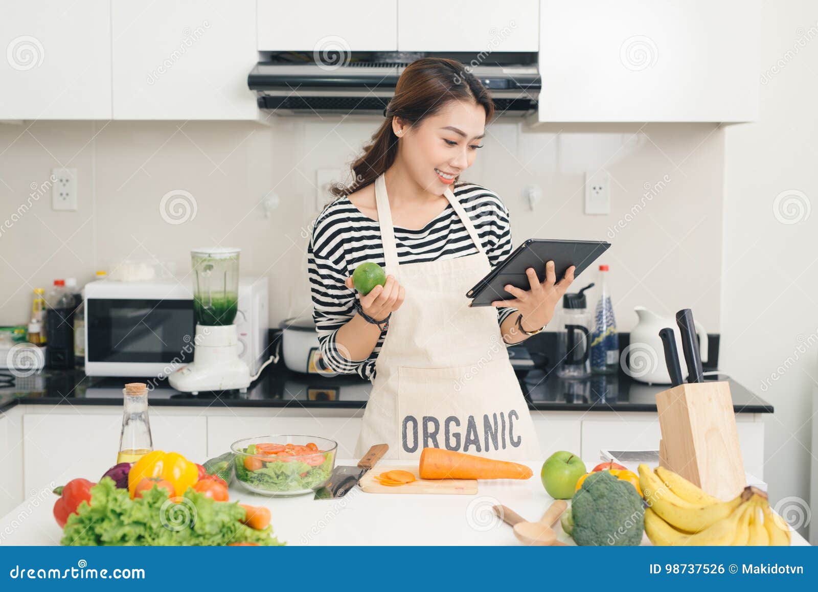 Young Asian Woman Using a Tablet Computer To Cook in Her Kitchen Stock ...