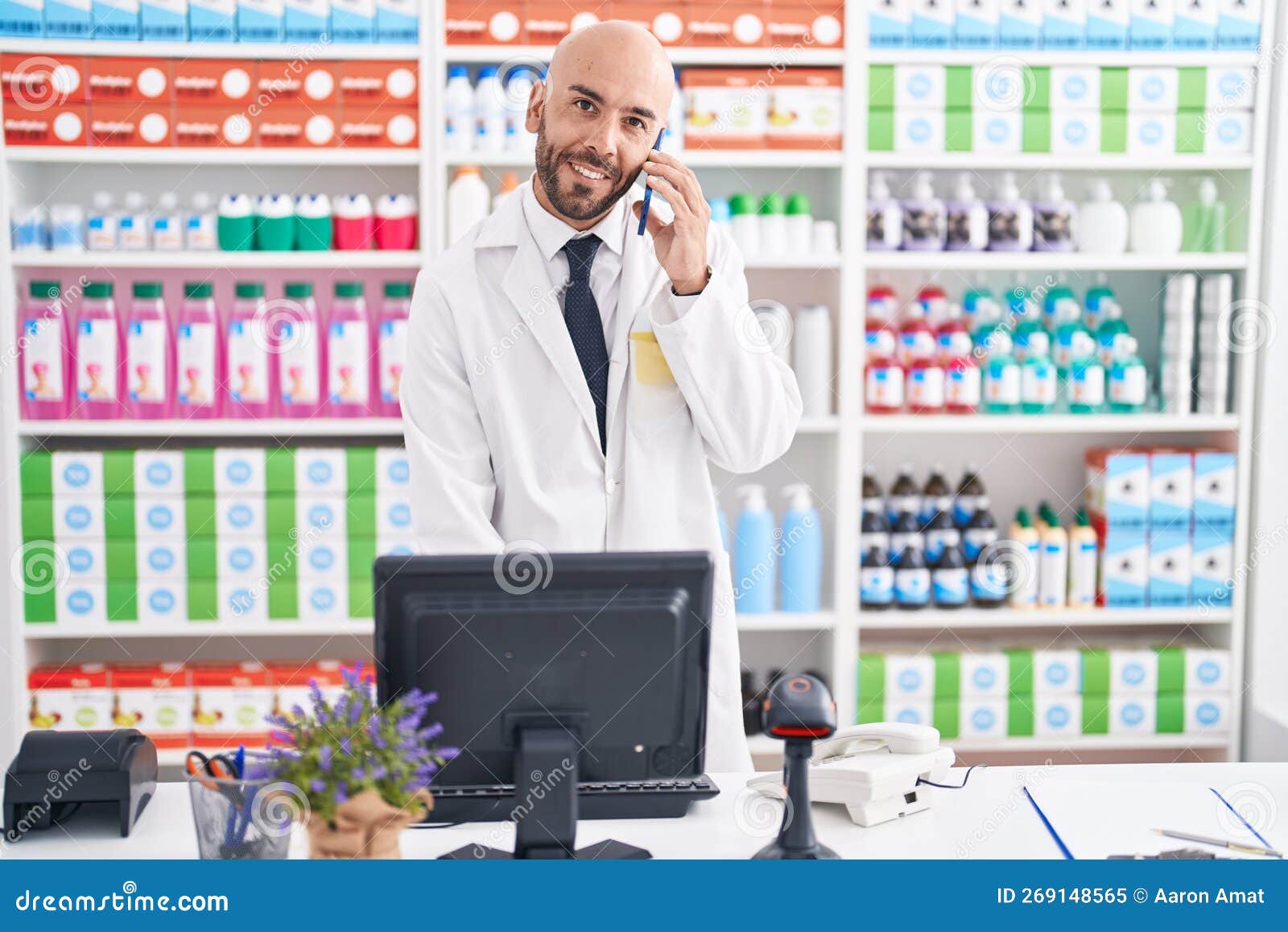 Young Bald Man Pharmacist Talking on Smartphone Using Computer at ...