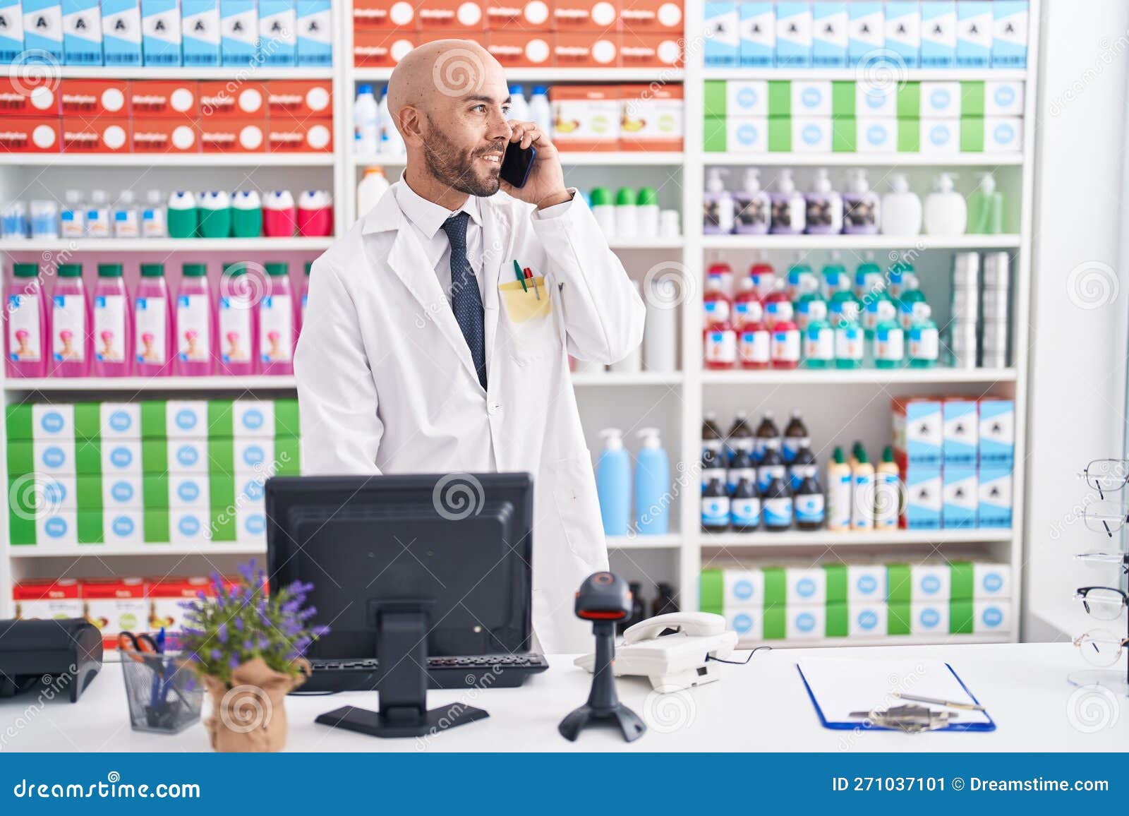 Young Bald Man Pharmacist Talking on Smartphone Using Computer at ...