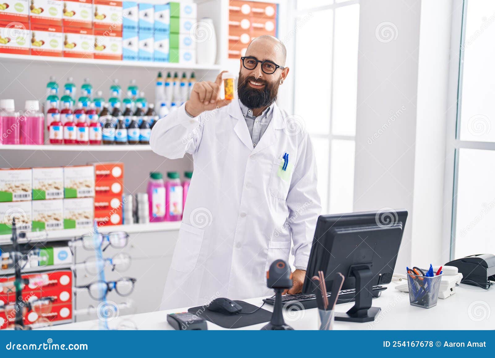 Young Bald Man Pharmacist Using Computer Holding Pills Bottle at ...
