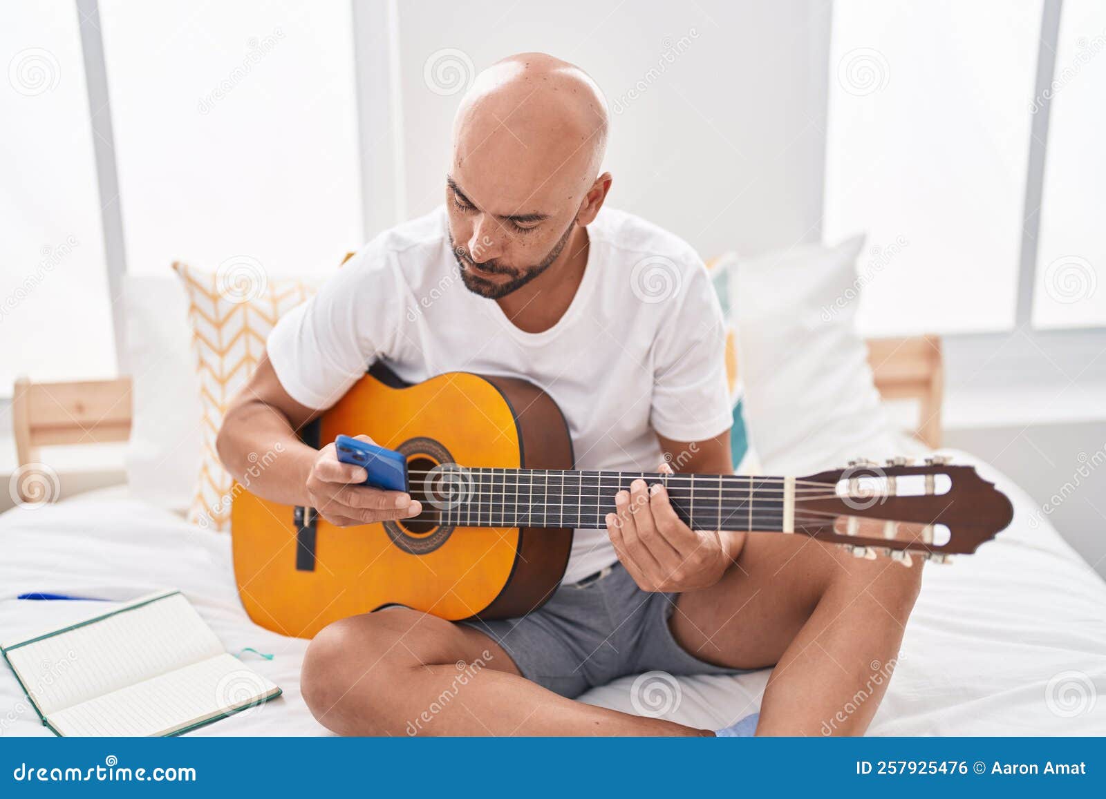 Young Bald Man Playing Classical Guitar Using Smartphone at Bedroom ...