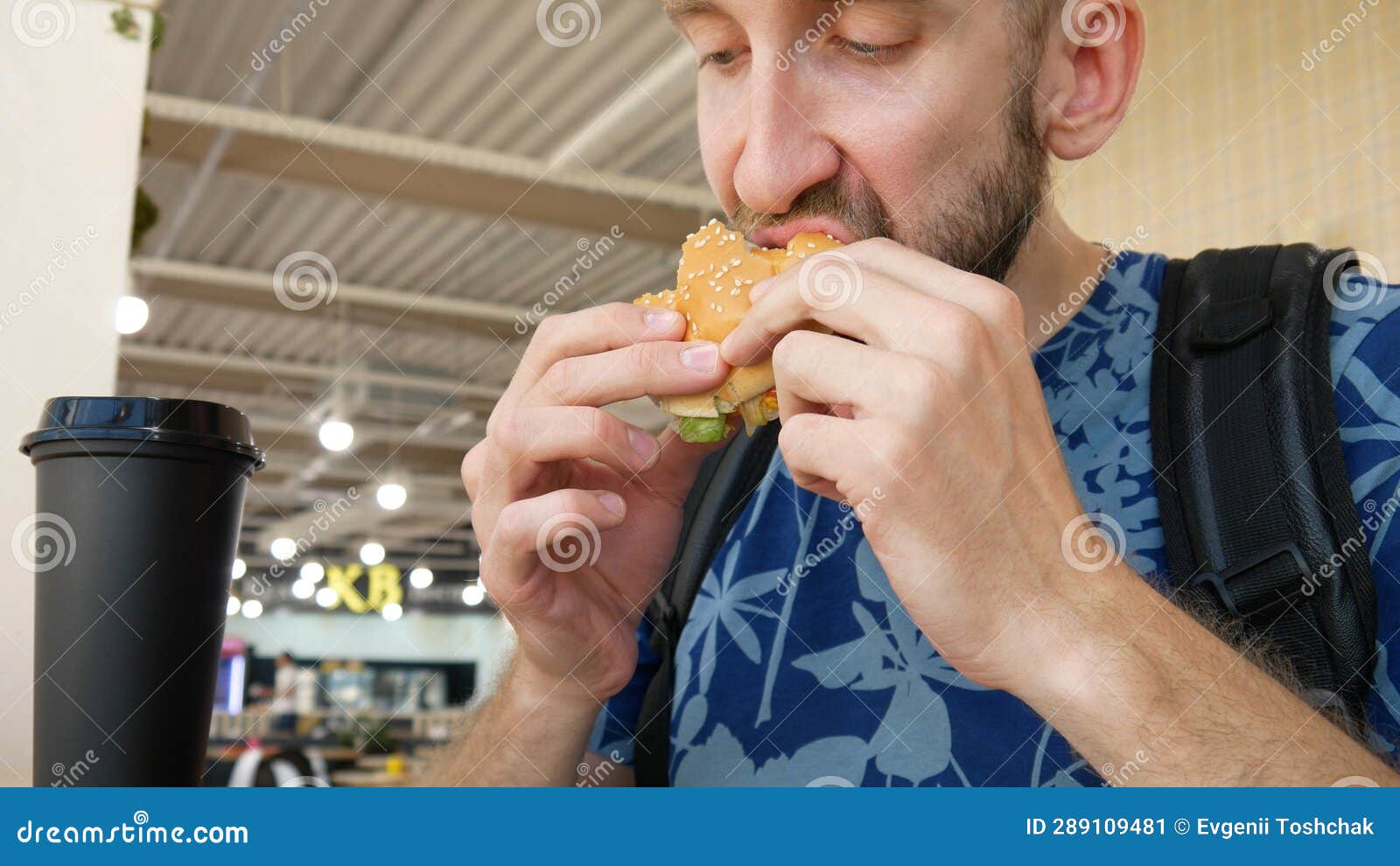 Close-up of a Young Man Biting a Hamburger at the Table in a Dinner ...