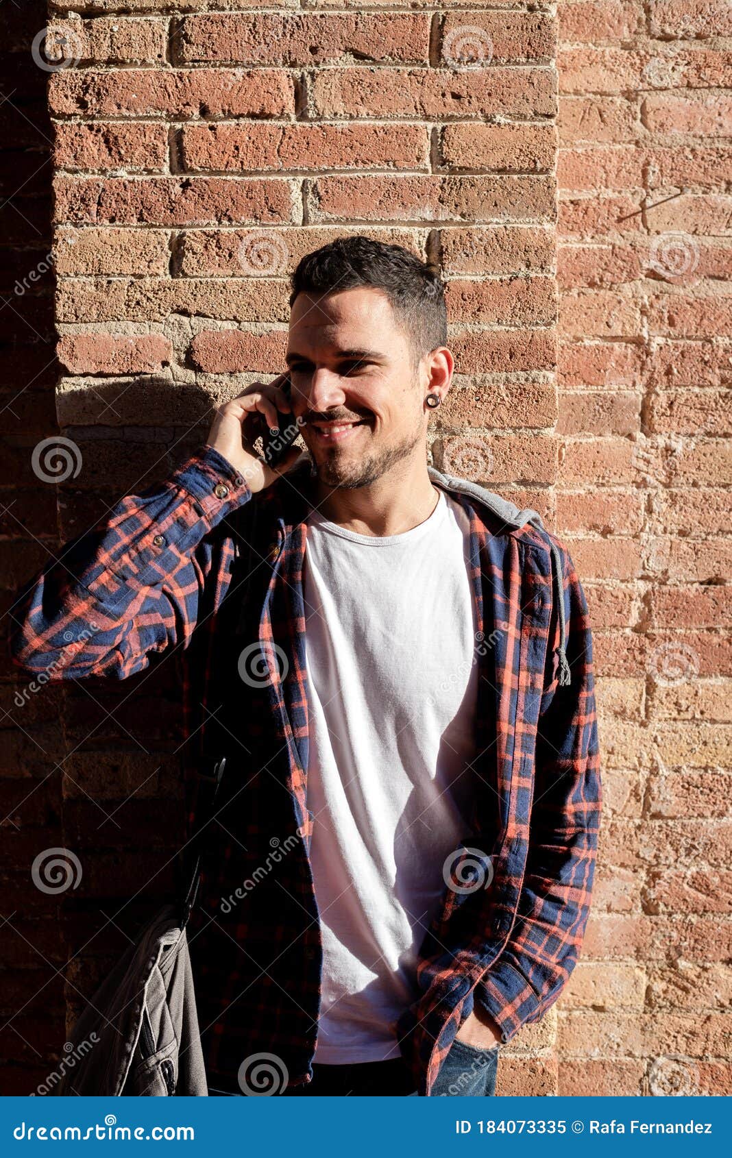 Young Bearded Man Leaning on a Bricked Wall while Using a Smartphone ...