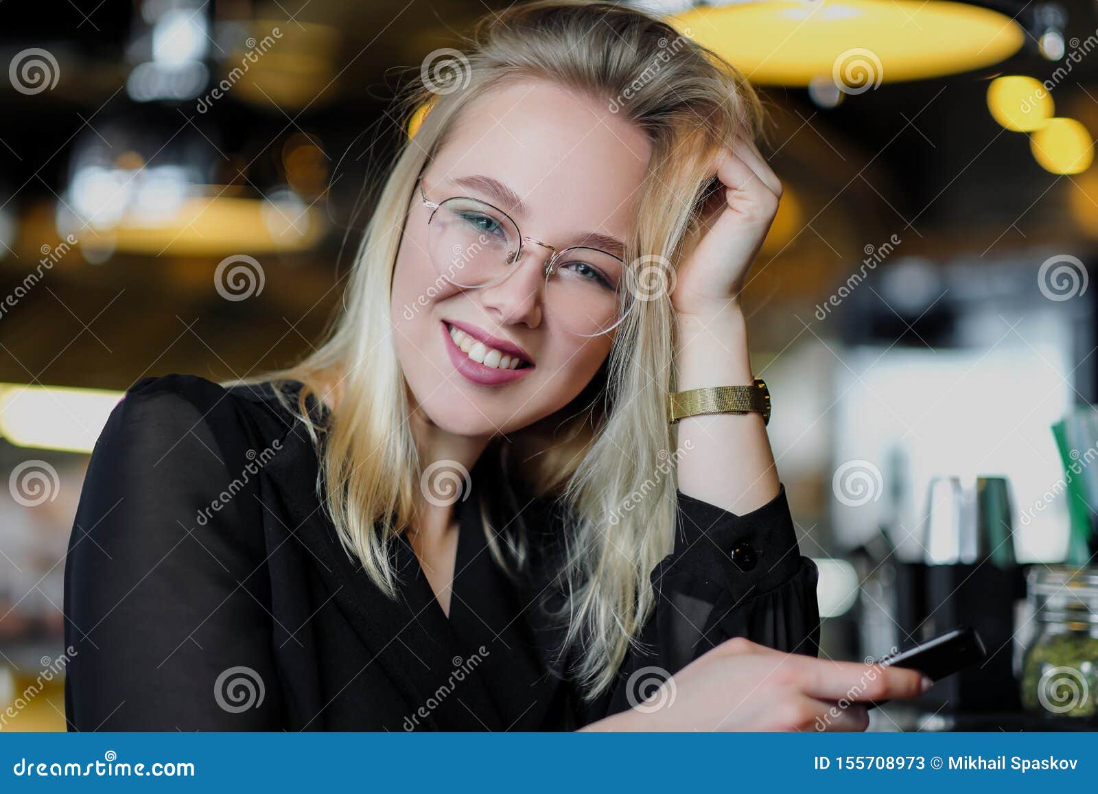 A Young Beautiful Blond Woman With Glasses Sits At The Bar In A Yellow