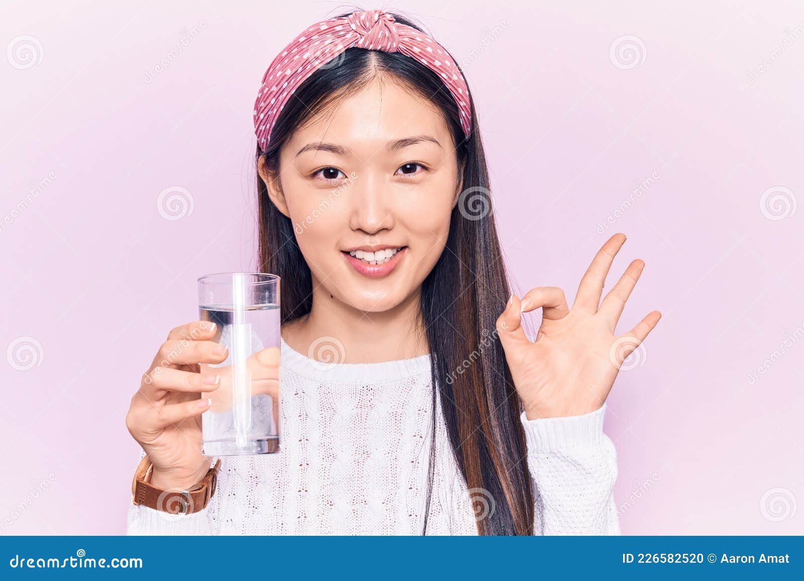 Young Beautiful Chinese Woman Drinking Glass Of Water Doing Ok Sign