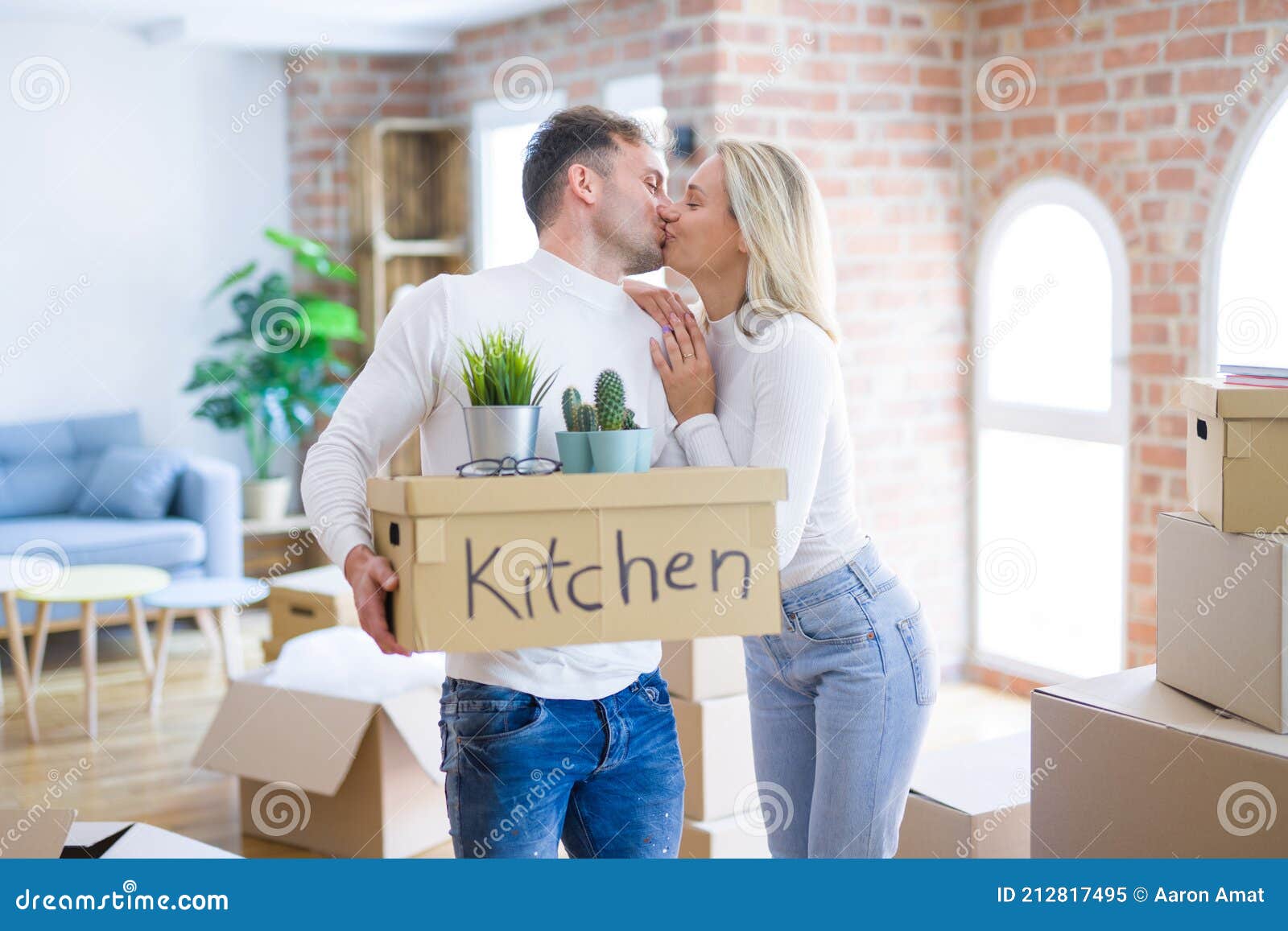 Young Beautiful Couple Kissing Moving Cardboard Boxes At New Home Stock
