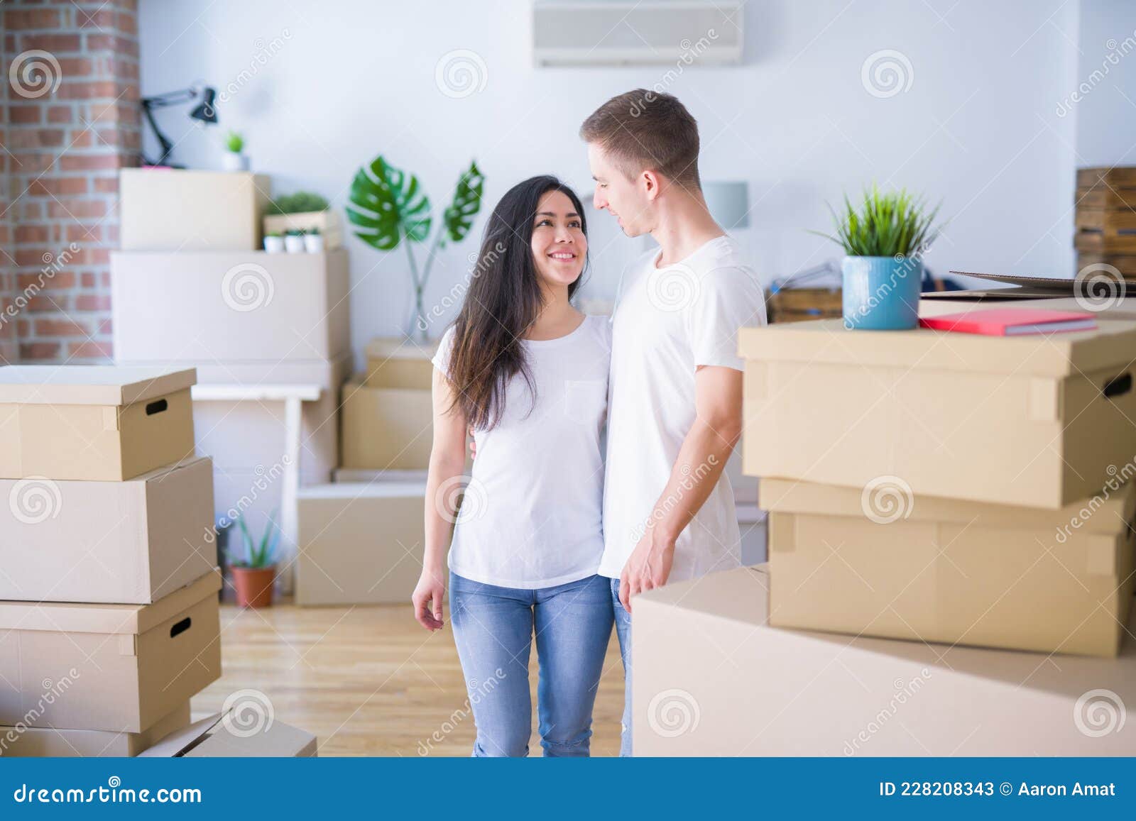 Young Beautiful Couple Standing At New Home Around Cardboard Boxes